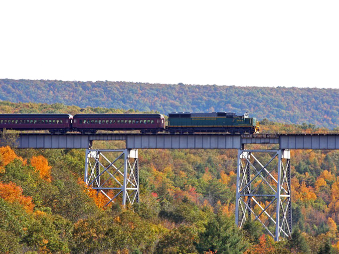 Engineering meets artistry as this train crosses high above the valley, threading through autumn's tapestry like a needle pulling golden thread.