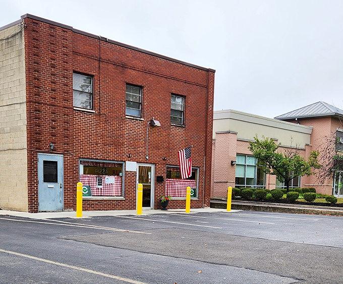 The humble exterior belies the culinary treasures within. Yellow parking bollards stand guard like sentinels protecting pizza perfection.