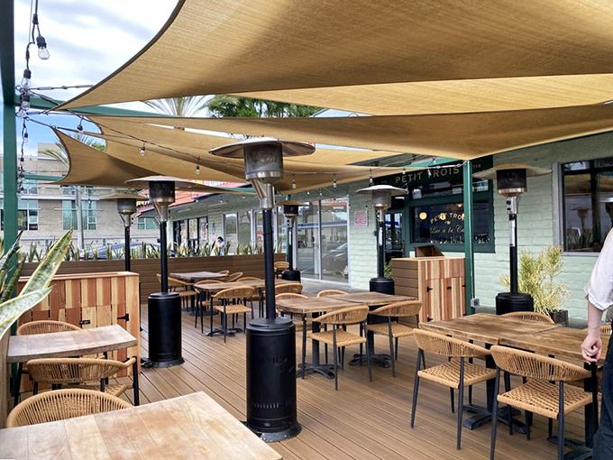 The outdoor dining area offers a breezy California twist on French ambiance. Canvas sails provide shade while wooden elements create a casual elegance perfect for lingering meals.