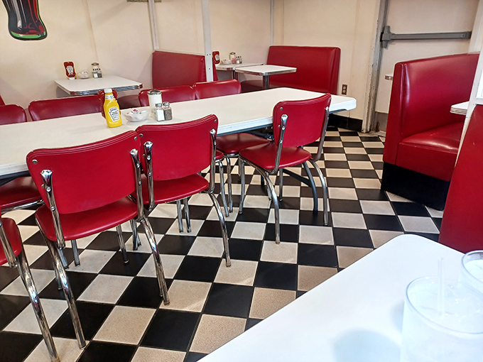 Red chairs wait patiently for the next shift of diners, their chrome legs gleaming against the checkerboard floor like pieces in a delicious game.