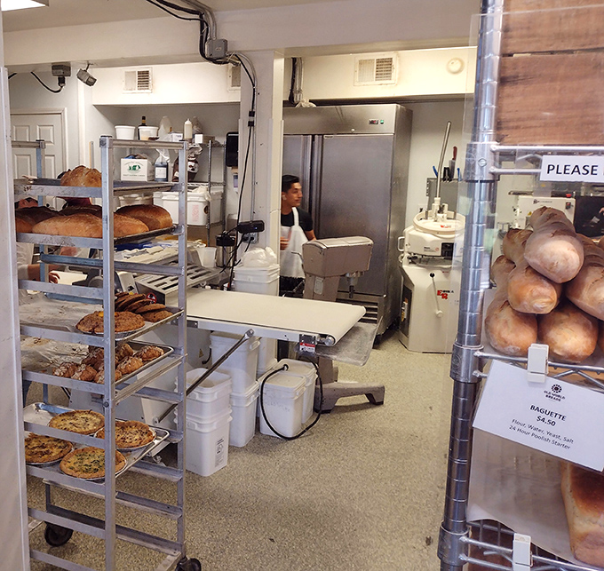 Behind the scenes where the magic happens. Racks of freshly baked treasures cool while bakers prepare the next batch of joy.