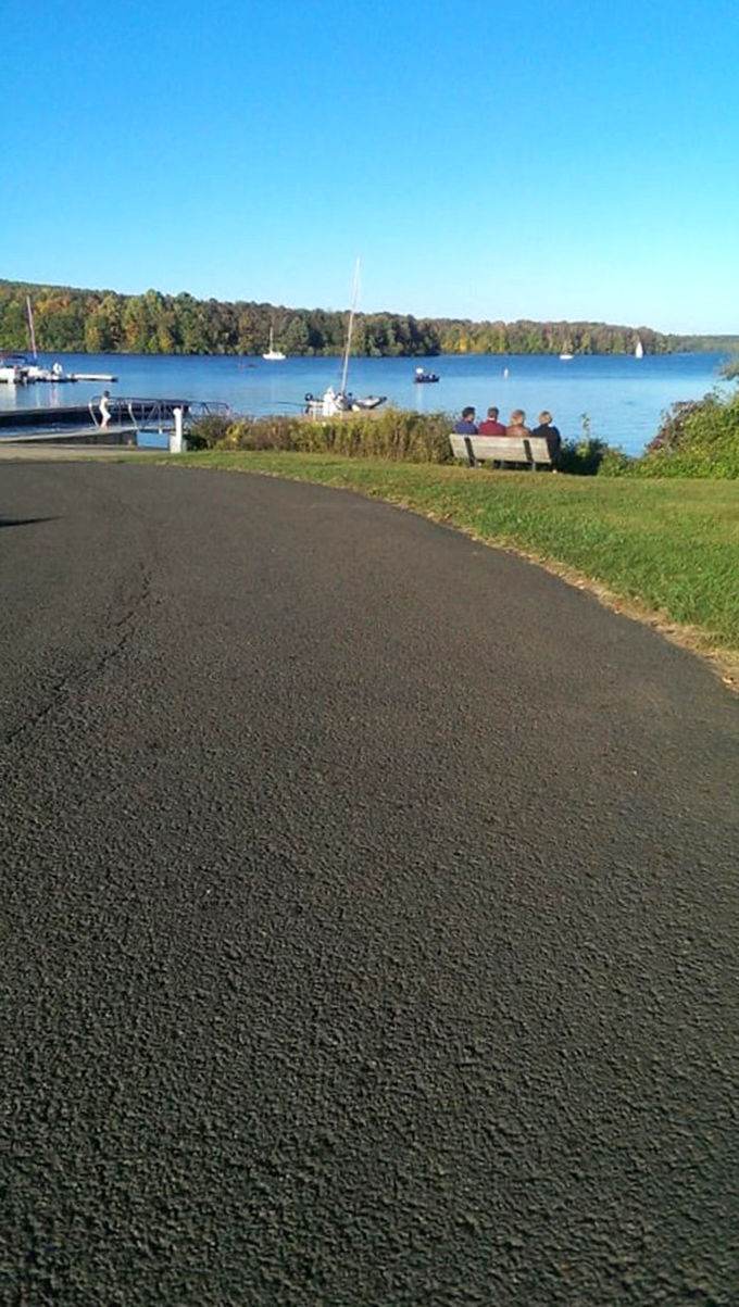 Waterfront serenity captured. This pathway curves alongside the lake, offering views that make smartphone cameras work overtime and Instagram filters unnecessary.
