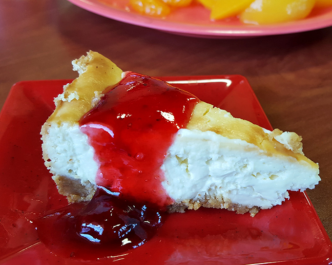 Cheesecake topped with ruby-red strawberry sauce &ndash; where cream cheese transcends to dessert divinity on a graham cracker throne.