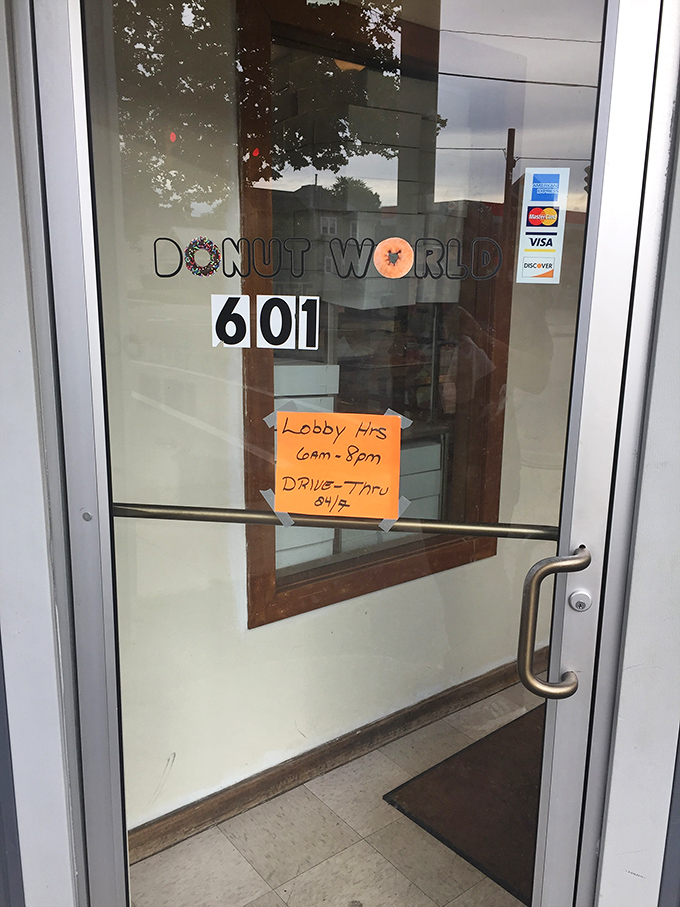 The entrance to Donut World—where the sign promises lobby hours of 6am-8pm and drive-thru until 9pm. Some doors lead to adventure; this one leads to donuts.
