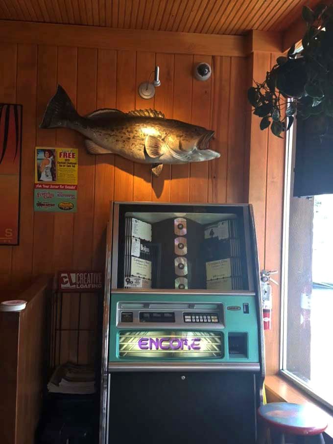 Where nostalgia meets seafood: a vintage jukebox shares space with a mounted fish, both treasures from a different era.
