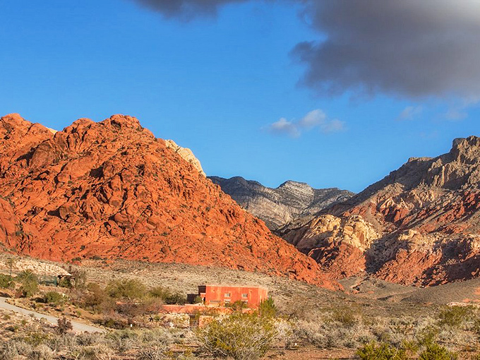 A lone structure stands sentinel among crimson cliffs. In this technicolor landscape, even buildings seem to adapt to nature's dramatic palette.