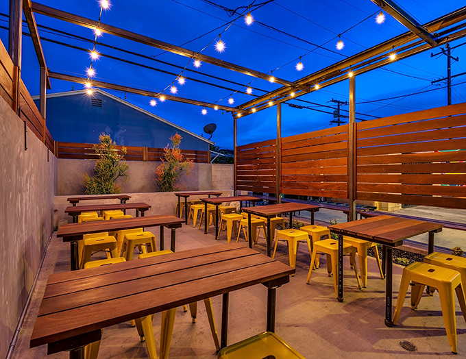 String lights twinkle above the outdoor patio, where yellow metal stools and wooden tables create the perfect stage for al fresco feasting.