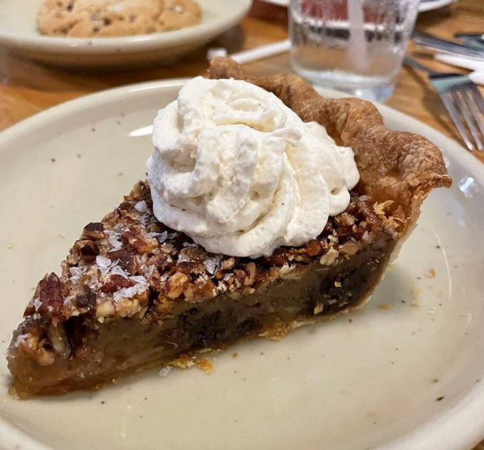 Pecan pie topped with a cloud of whipped cream &ndash; the kind of dessert that makes you consider ordering a second slice before finishing the first.