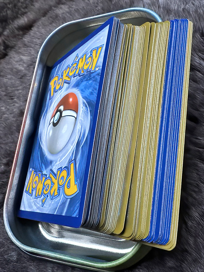 Pok&eacute;mon cards nestled in their metal tin&mdash;where childhood nostalgia meets adult collecting obsession in a perfect storm of "gotta catch 'em all."