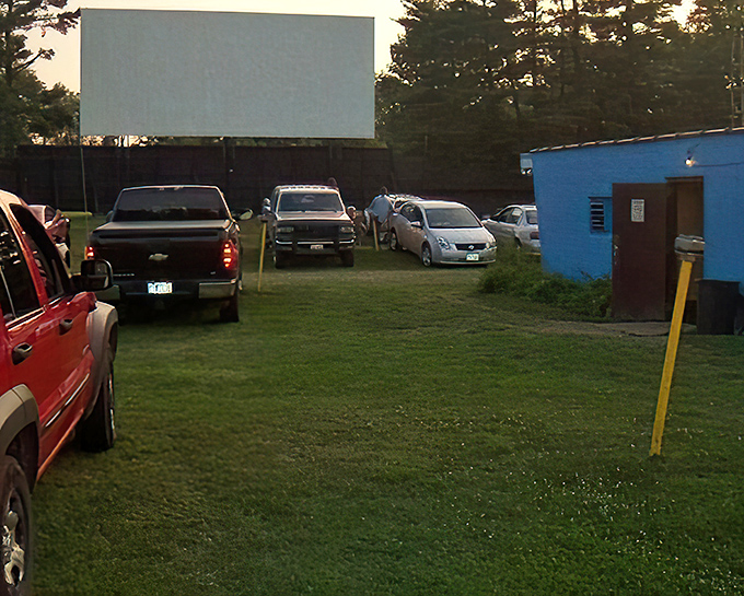 As darkness falls, headlights guide latecomers to their spots. The blue concession building glows like a beacon for those craving last-minute snacks.