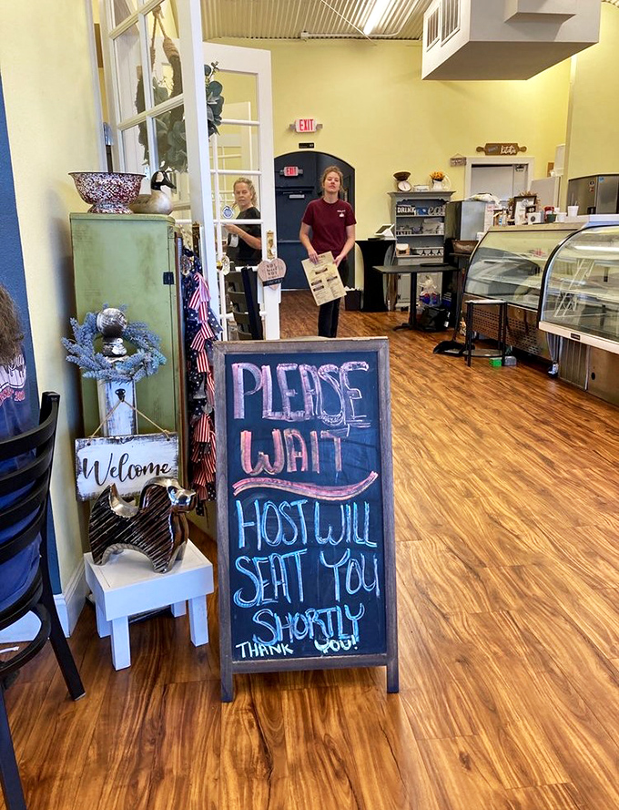 A chalkboard greeting that perfectly captures diner humor: "Please wait, host will seat you shortly" &ndash; directness wrapped in chalk-dusted charm.