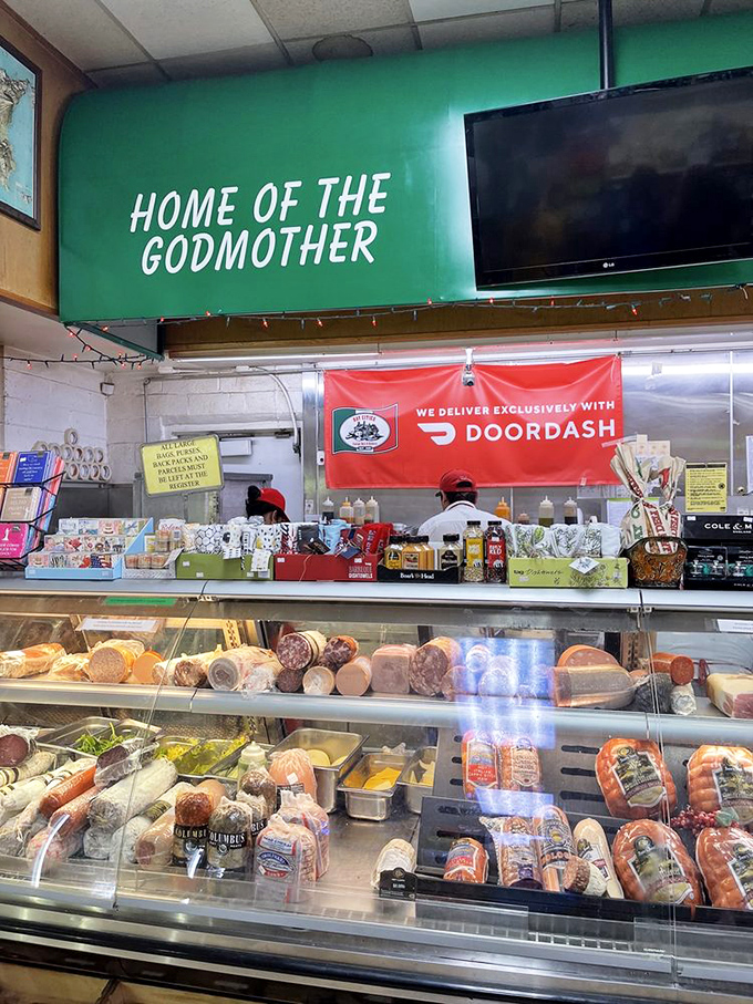 Under the "HOME OF THE GODMOTHER" sign, deli artisans work their magic, transforming simple ingredients into legendary sandwiches.