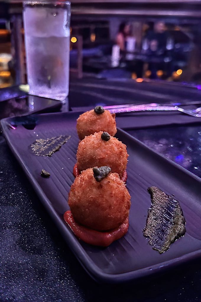 These aren't just arancini—they're edible art, perfectly golden spheres resting on vibrant sauce that looks suspiciously like something Dracula might enjoy.
