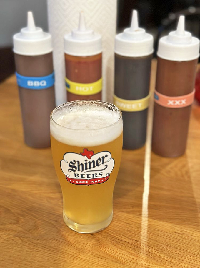 A frosty Shiner Beer standing guard over sauce bottles&mdash;because great barbecue deserves a proper liquid companion on its journey.