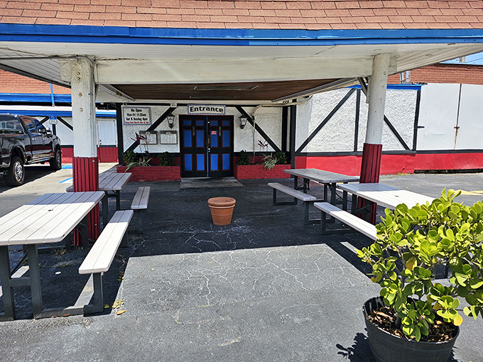 The entrance beckons with its distinctive red, white, and black color scheme. Outdoor picnic tables hint at the gemütlichkeit waiting just beyond those doors.