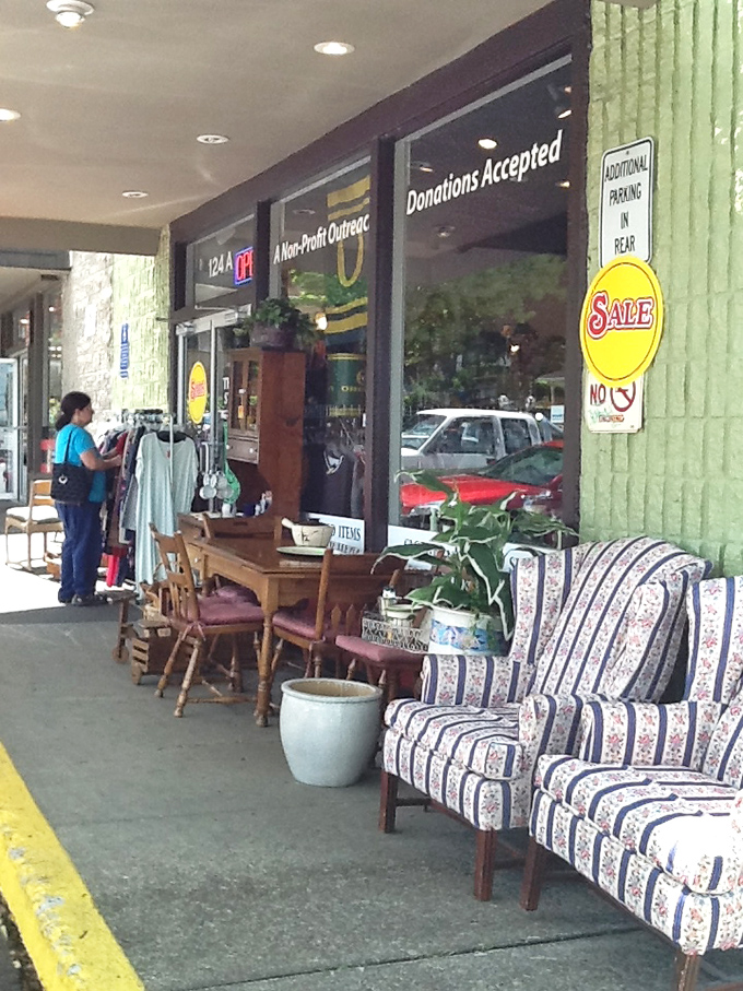 Sidewalk showcase of quality furniture waiting for new homes – from striped armchairs to wooden dining sets, treasures spill outside on nice days.