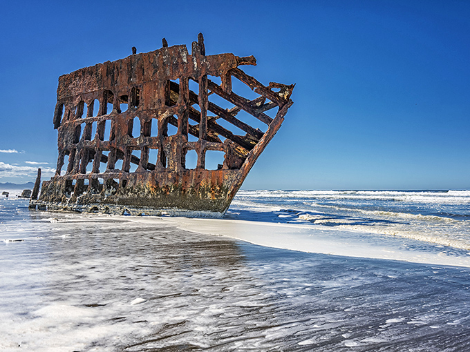 When high tide embraces the Peter Iredale, the boundary between past and present blurs in a frothy dance of waves and weathered metal.