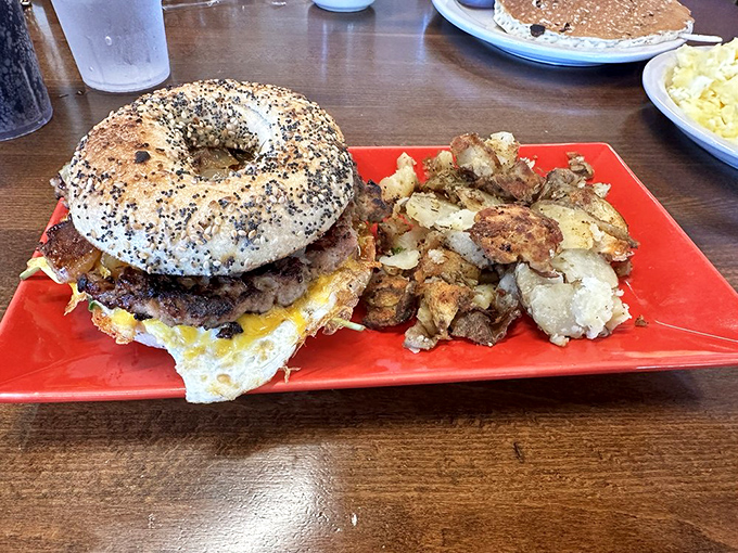 The breakfast sandwich on a bagel—where morning meets innovation on a red plate—proves that good things come in round packages with a side of perfectly seasoned potatoes.