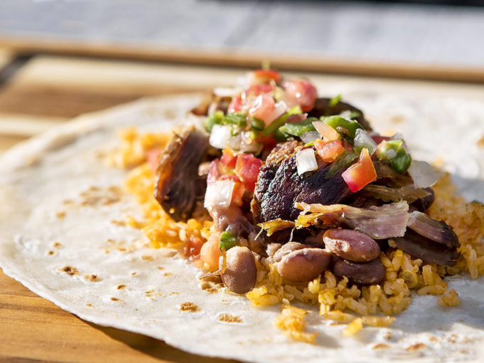 A tortilla unfurled reveals its treasure &ndash; perfectly seasoned carnitas nestled with rice and beans, topped with fresh pico.