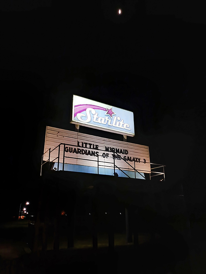 The marquee glows like a beacon in the night, advertising "Little Mermaid" and "Guardians of the Galaxy 3" under a watchful moon.