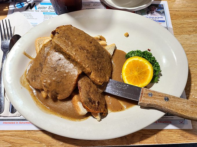 Meatloaf that doesn't just sit on the plate – it commands respect with its rich gravy and that perfect orange slice garnish.