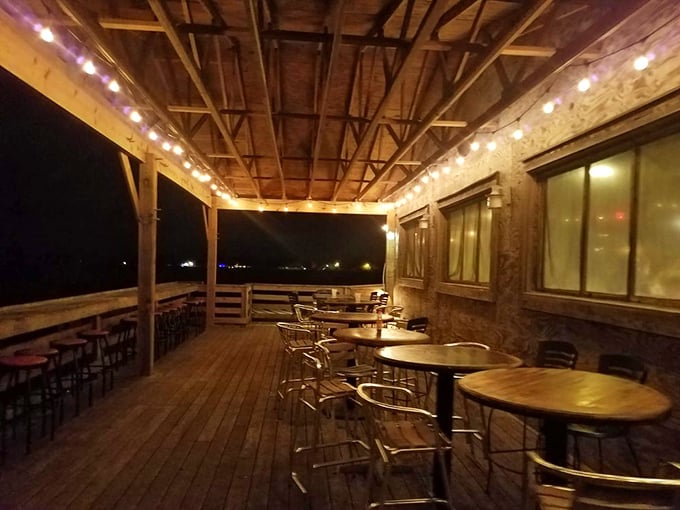 This cozy, string-lit outdoor patio with wooden floors and metal seating offers a warm and inviting spot for evening dining or drinks.