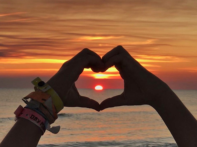 Hands forming a heart against a fiery sunset&mdash;the universal symbol for "sorry boss, I'm extending my vacation another week."