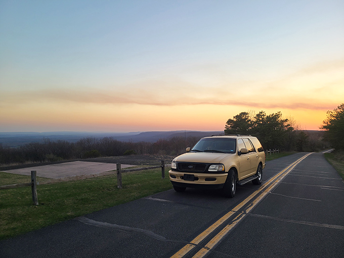 Sunset paints the sky in watercolor washes, while a lone vehicle witnesses nature's daily masterpiece performance.