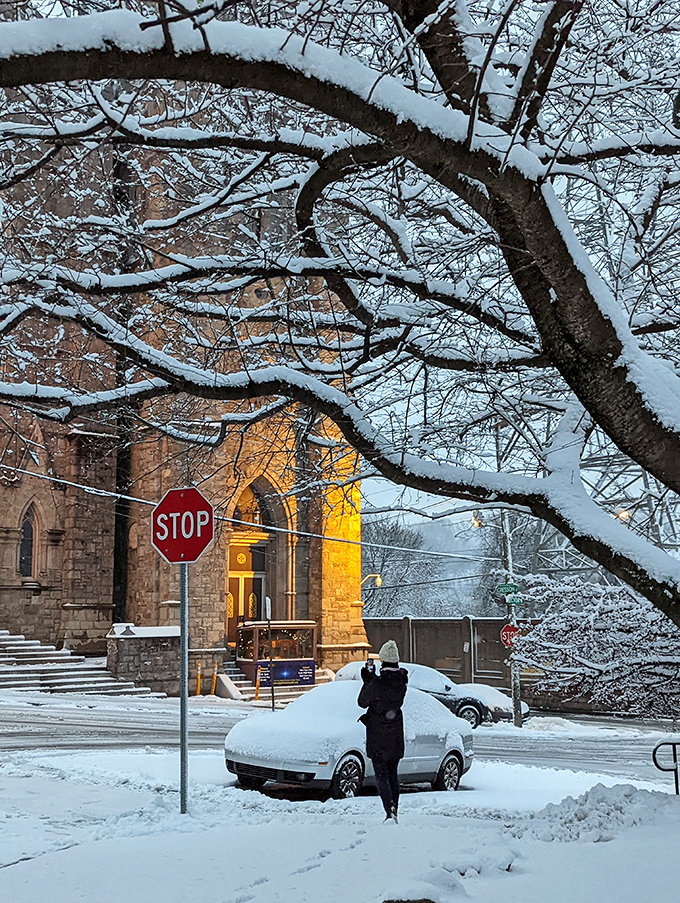 Snow blankets Manayunk in winter magic, the stone church glowing like a beacon through crystalline branches. Even stop signs look poetic in this seasonal transformation.