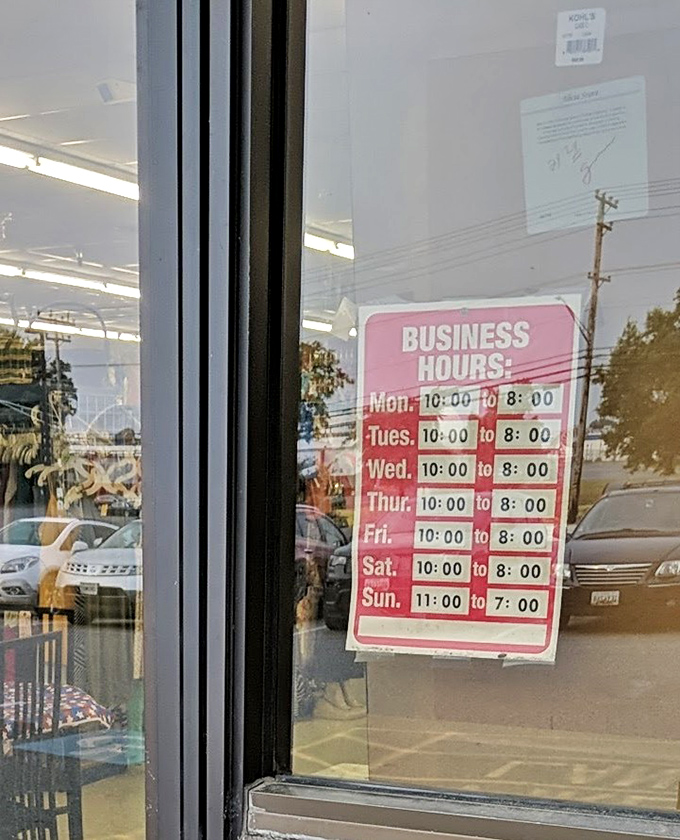 The hours posted like a promise: seven days a week of treasure hunting possibilities. The reflection shows eager shoppers already gathering.