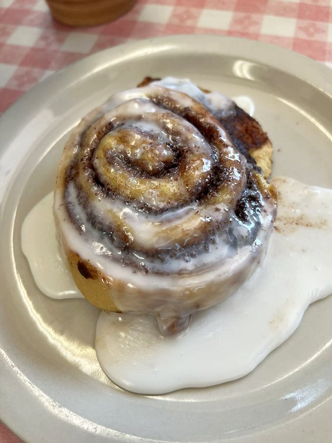 The cinnamon roll doesn't merely arrive&mdash;it makes a grand entrance, swimming in a pool of icing that transforms your coffee into the perfect supporting actor.