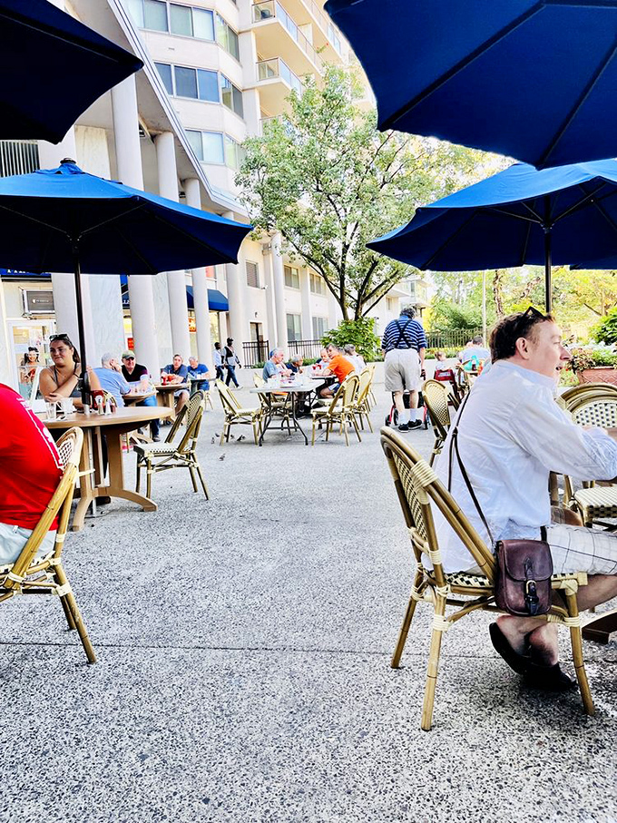 The outdoor dining area buzzes with conversation and clinking glasses. Under those blue umbrellas, strangers become neighbors over shared meals.