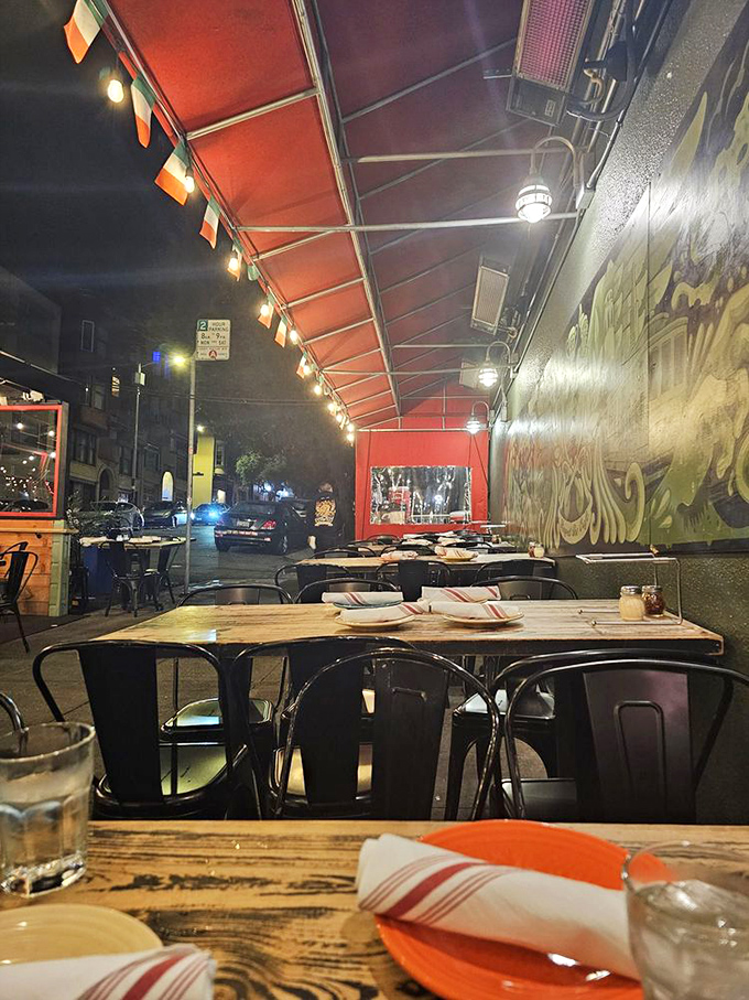 As night falls, the outdoor seating transforms into a cozy urban oasis where the red glow of heaters matches the warmth of the pizza-induced happiness around each table.