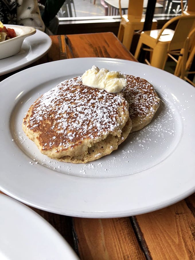 Pancakes that achieve the impossible: cloud-like fluffiness with golden edges, dusted with powdered sugar that makes every bite taste like a celebration.