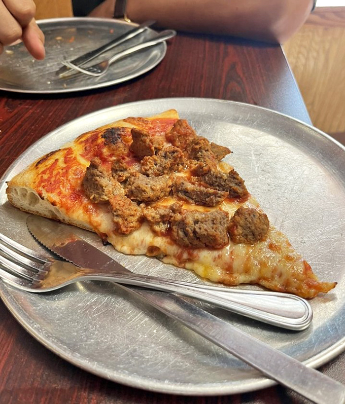 This sausage pizza slice isn't just food; it's a commitment to excellence that requires both knife and fork to fully appreciate.