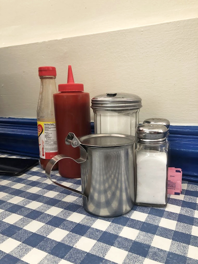 The holy trinity of diner condiments&mdash;ketchup, sugar, and salt&mdash;standing ready on blue-checked tablecloths like old friends waiting to enhance your breakfast experience.