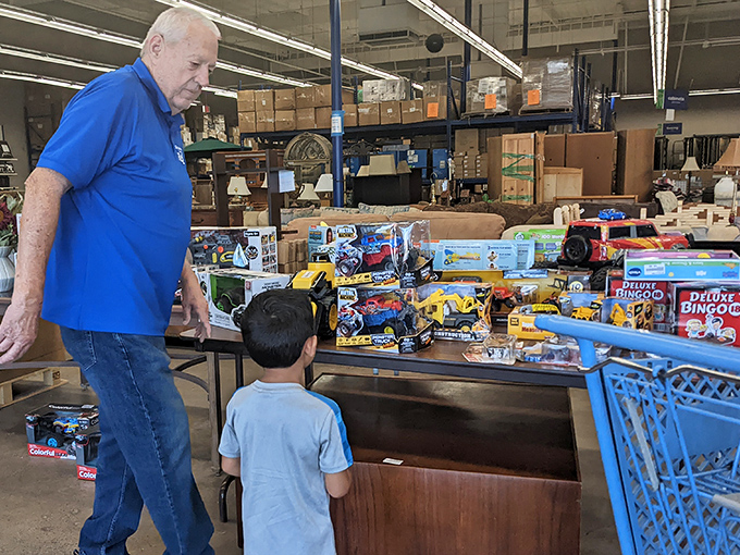 Intergenerational joy as this volunteer shares the toy section's treasures with a young shopper, proving ReStore magic works for all ages.