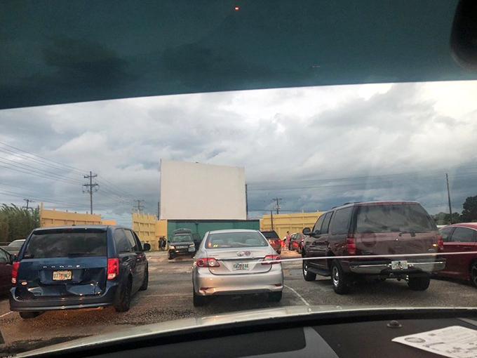 The view from your windshield: cars, anticipation, and a blank screen waiting to burst into Technicolor life as dusk settles.