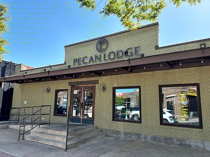 The Pecan Lodge storefront beckons like a temple of smoke. That tan brick exterior hides treasures worth every minute in line.