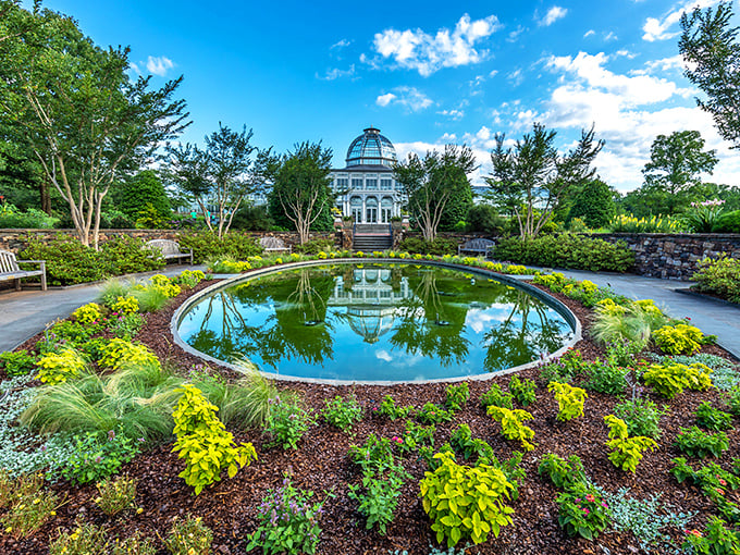 Nature's perfect mirror: the Conservatory reflects in the circular pond, creating a double dose of architectural splendor surrounded by vibrant plantings.