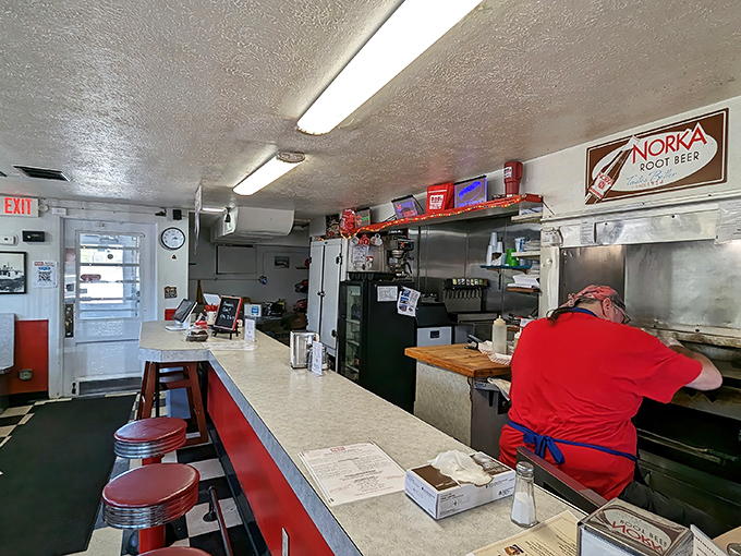 The heart of burger artistry happens behind this counter, where decades of seasoning on that flat-top grill have created a flavor no fancy restaurant can replicate. 