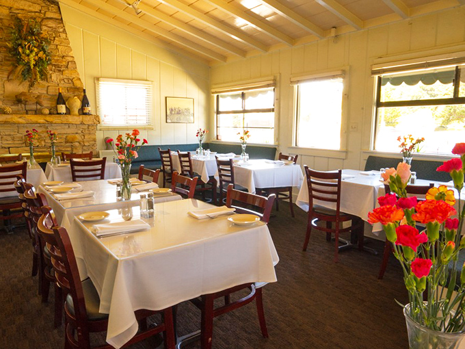White tablecloths meet rustic stone fireplace in this cozy dining room where fresh flowers add splashes of color to conversations about seafood.
