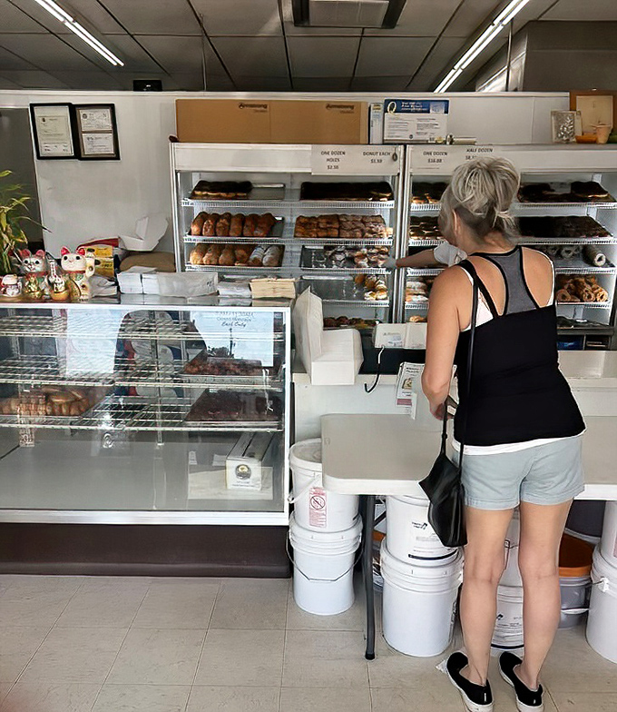A customer contemplates life's sweetest decisions at the simple, no-nonsense counter. The display cases speak volumes about priorities here: donuts first, everything else second.