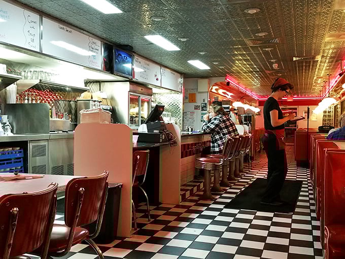 Classic black and white checkered floors lead you past cherry-red counter stools where regulars perch like birds on a wire, watching breakfast magic unfold.