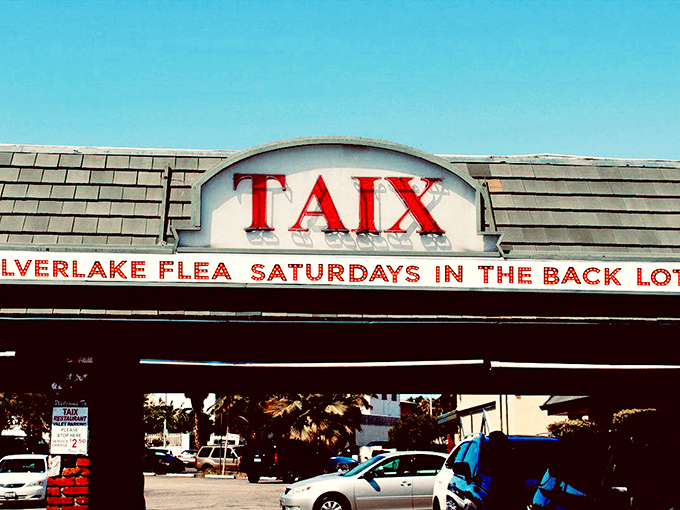 The iconic Taix sign stands as a beacon for weekend bargain seekers, announcing the flea market's presence with vintage charm and California sunshine.