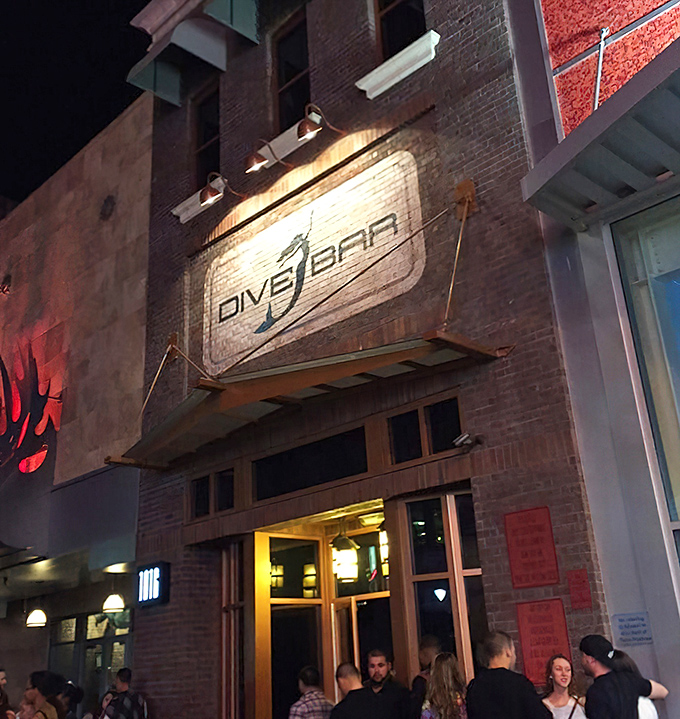 Night falls on K Street, but Dive Bar's glowing sign serves as a lighthouse for thirsty adventurers seeking underwater enchantment.