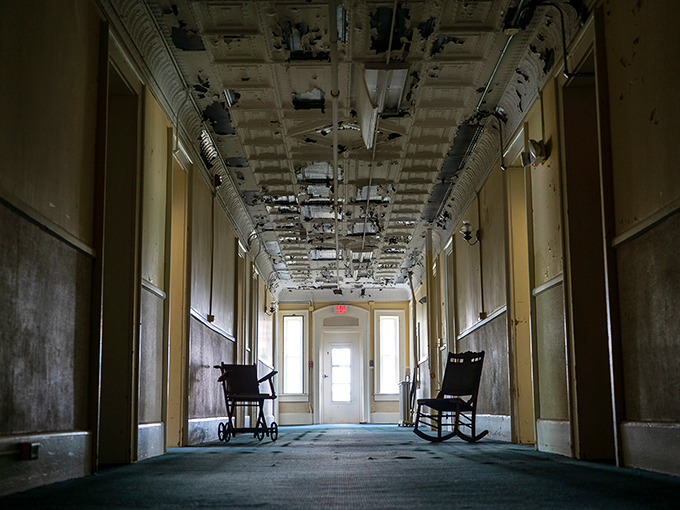 Time stands frozen in this haunting corridor where wheelchairs and rocking chairs wait patiently for occupants who checked out decades ago.
