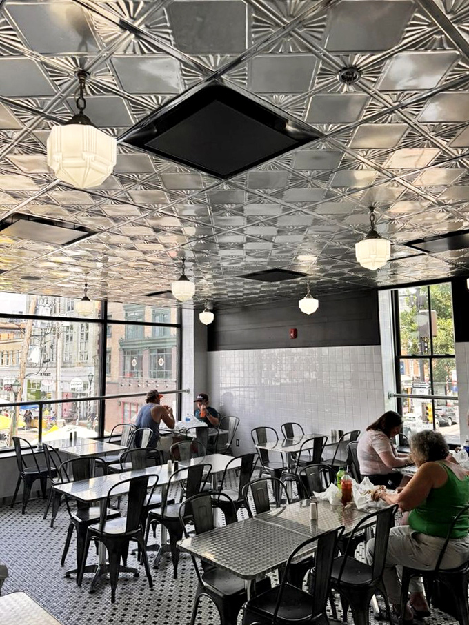 Vintage pressed tin ceilings and globe lights hover above metal tables where strangers become friends, united by the universal language of cheesesteak appreciation.