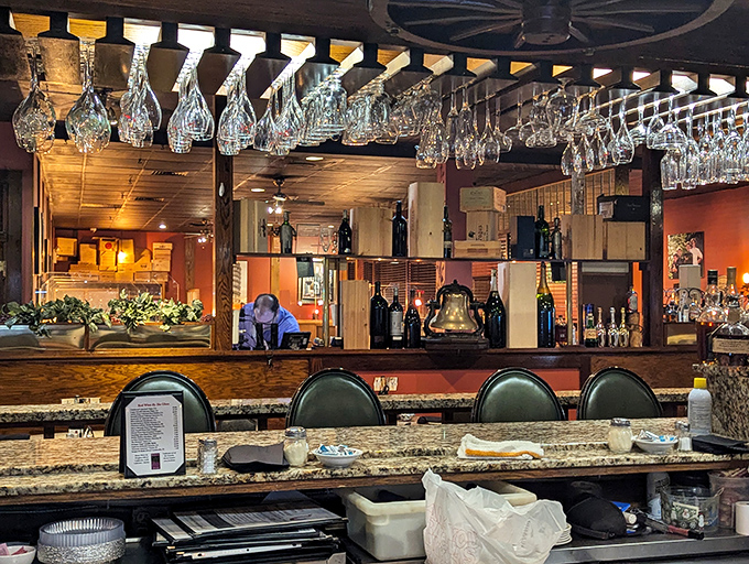 Wine glasses suspended from the ceiling create a crystal chandelier effect, while the warm wooden bar beckons with promises of perfectly mixed manhattans and local gossip.