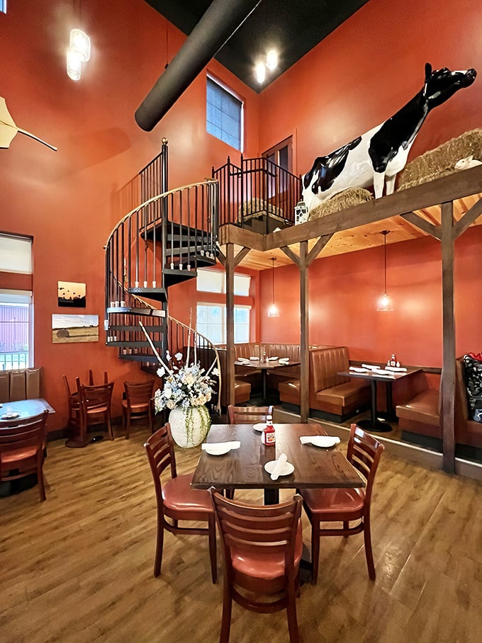 A spiral staircase winds through the warm terracotta interior, while a watchful Holstein cow statue keeps an eye on diners from its wooden perch.